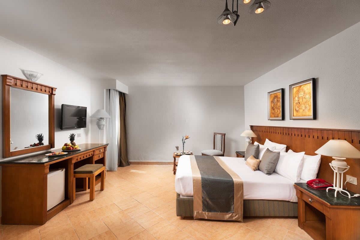 Quarto de hotel com cama, escrivaninha, cadeira e televisão.