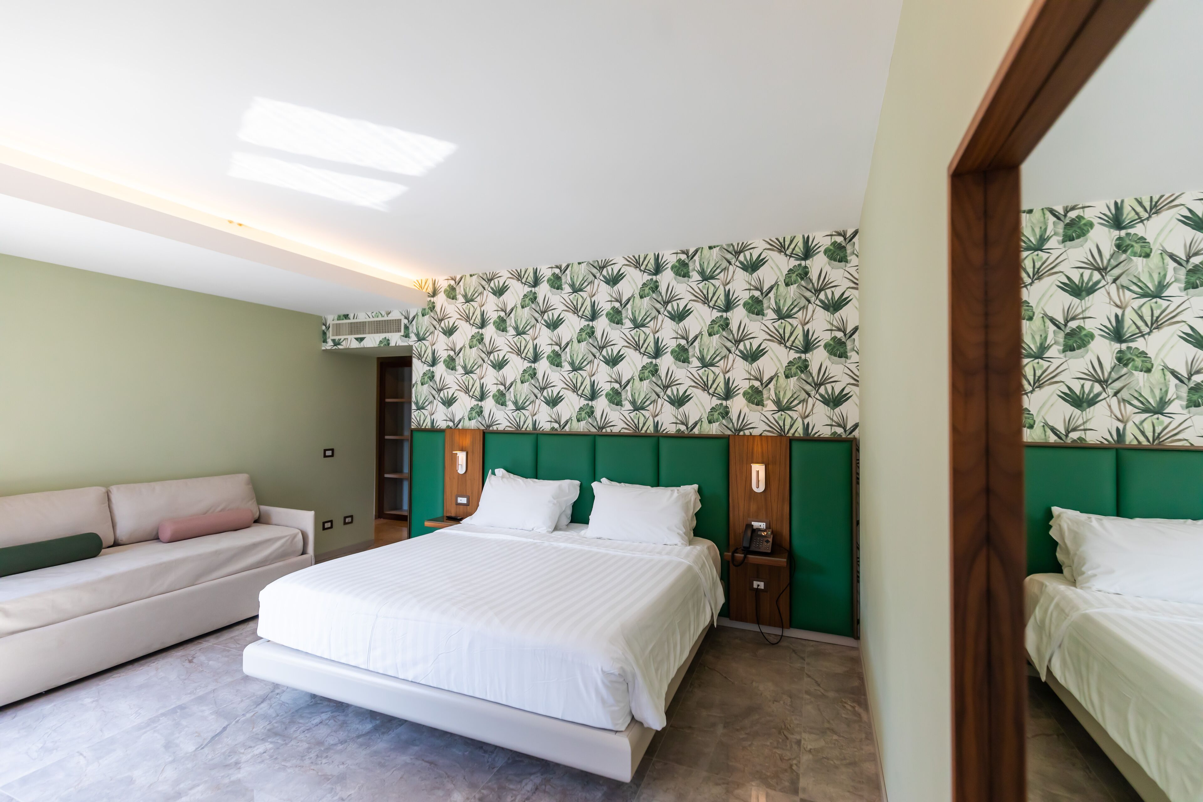 Quarto com cama, sofá, cabeceira verde e papel de parede estampado.