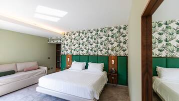 Quarto com cama, sofá, cabeceira verde e papel de parede estampado.