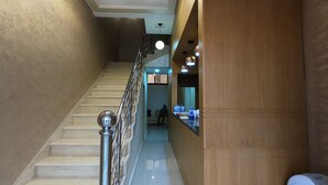 Uma escadaria com corrimão de metal, piso polido e um espelho na parede refletindo uma pessoa.