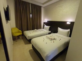 Quarto de hotel com duas camas, uma cadeira amarela e uma televisão de tela plana fixada na parede.