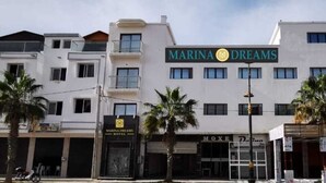 Um hotel chamado 'Marina Dreams' com fachada moderna, várias varandas e palmeiras na frente.