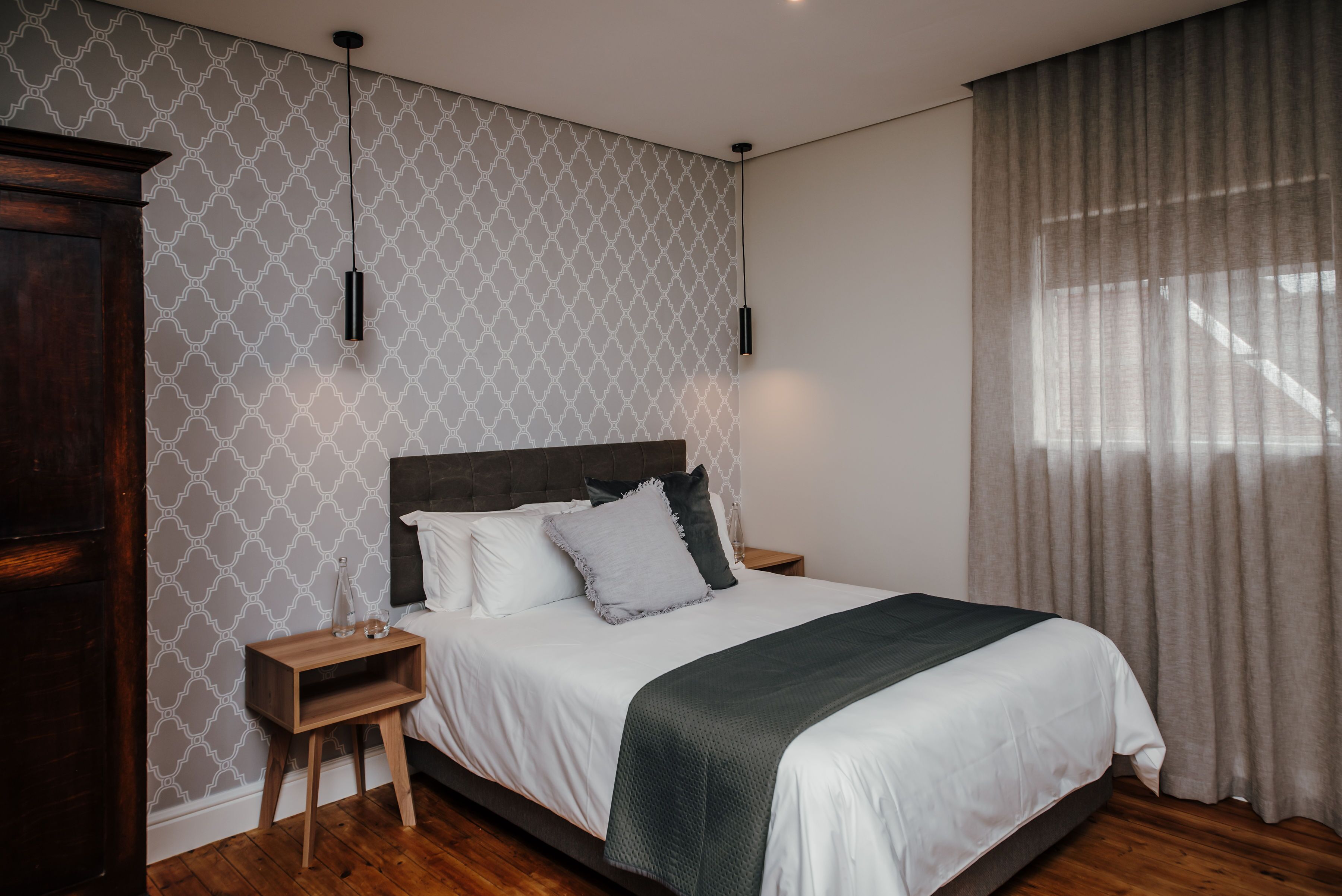 Quarto com cama, mesa de cabeceira de madeira e parede estampada.