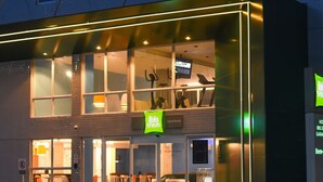 Um edifício moderno com fachada de vidro, uma placa indicando "IBIS Styles" e uma escadaria visível que leva a um andar superior.