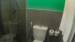 Casa de banho com chuveiro de cabine de vidro, sanita e dois rolos de papel higiénico.