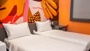 Quarto de hotel com duas camas de solteiro, uma mesinha de cabeceira com telefone e um mural abstrato e colorido na parede.