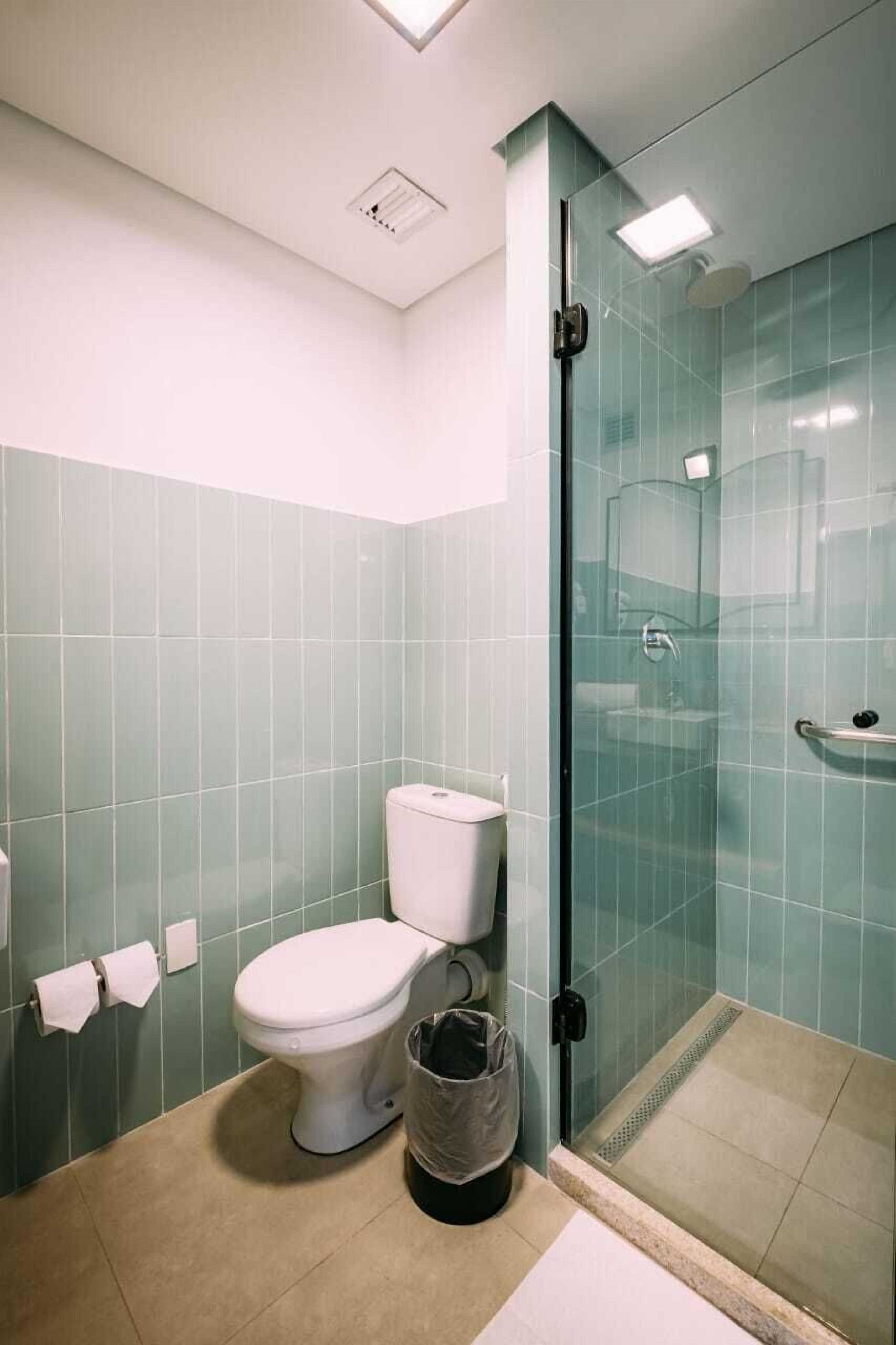 Casa de banho com sanita, um lixo, cabine de duche em vidro e um porta-toalhas.