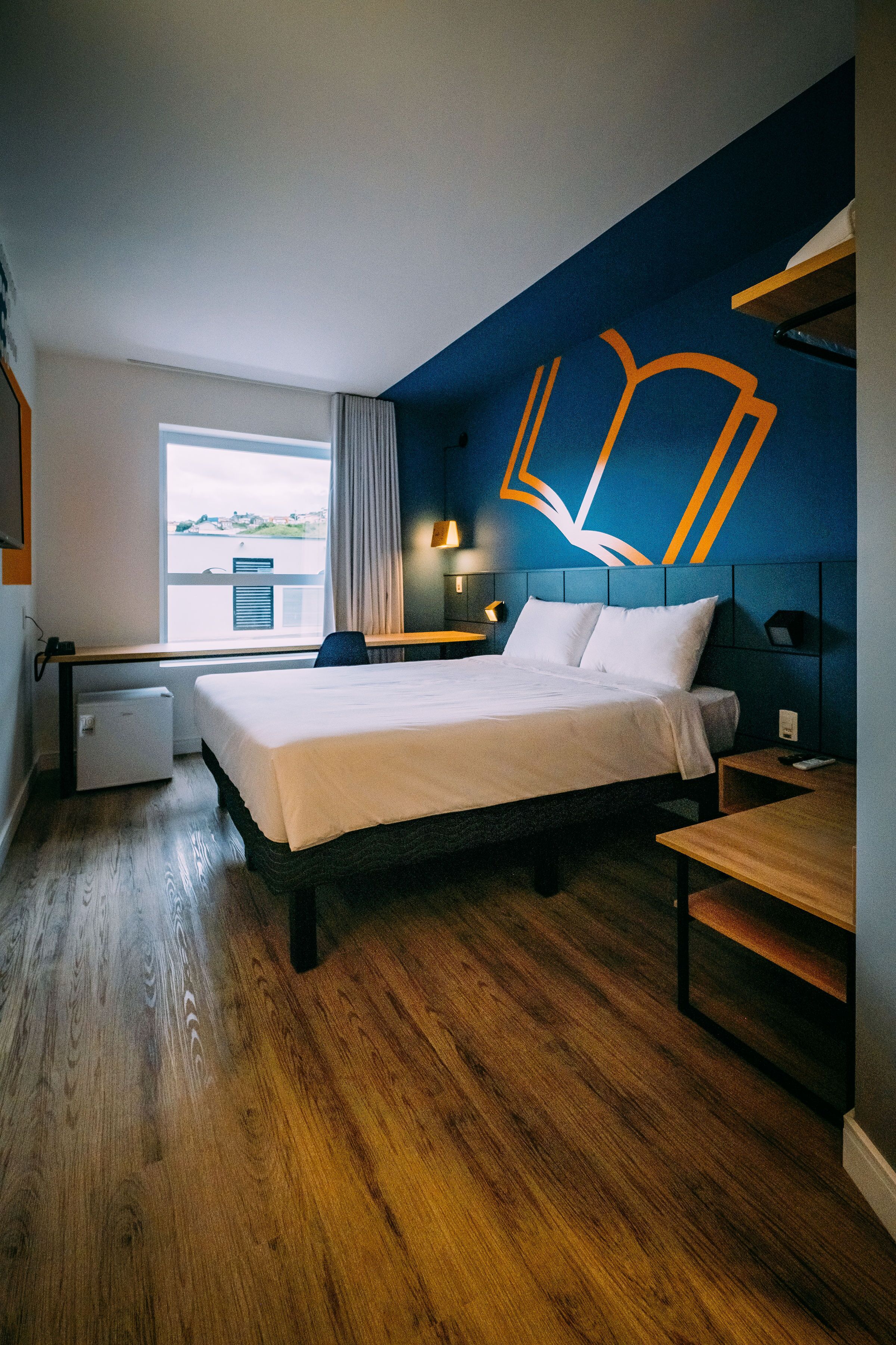 Quarto de hotel moderno com uma cama grande, uma escrivaninha e vista para o exterior.