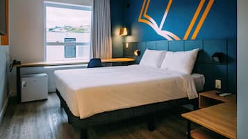Quarto de hotel moderno com uma cama grande, uma escrivaninha e vista para o exterior.