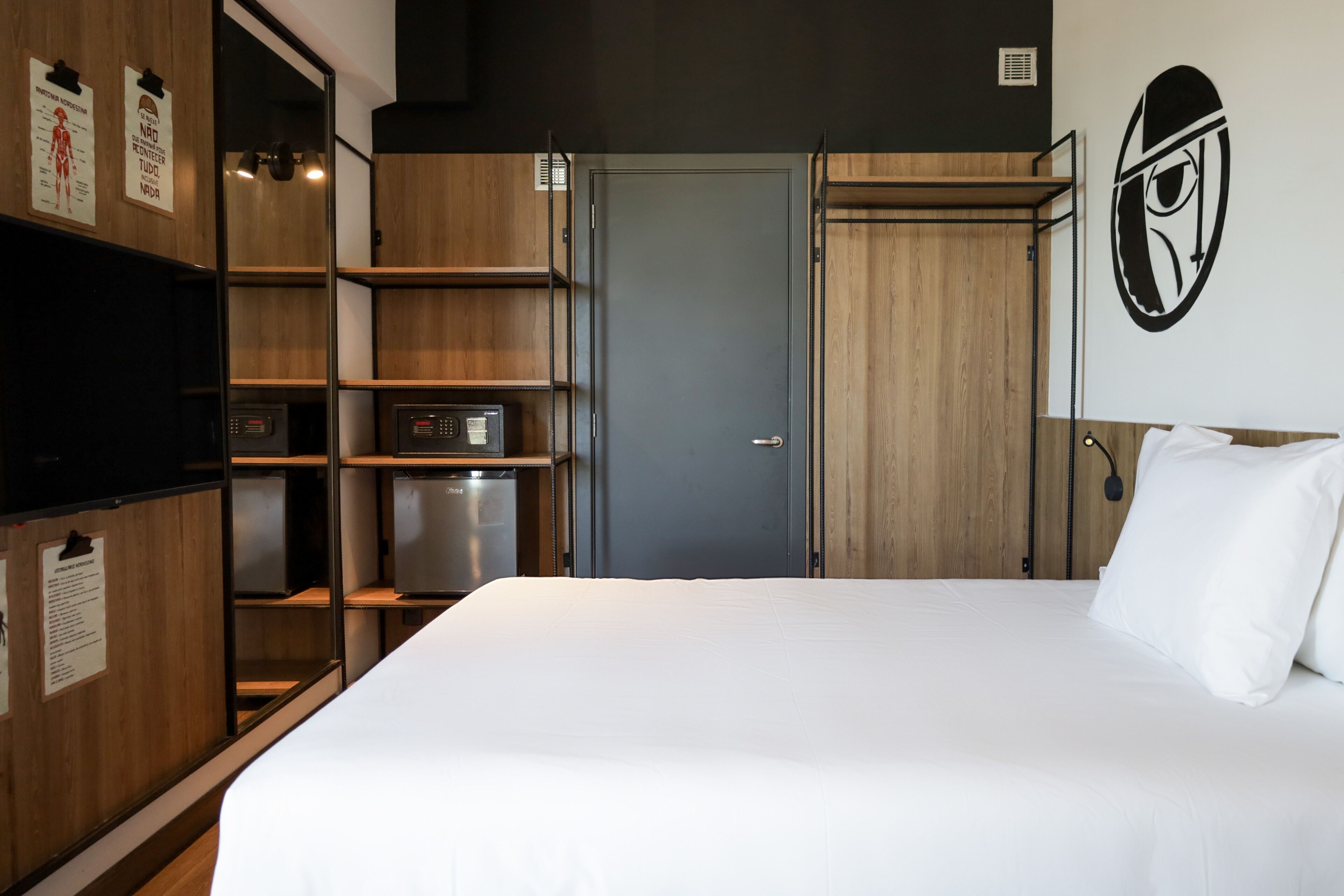 Quarto de hotel com uma cama grande, guarda-roupa de madeira e uma pequena cozinha.