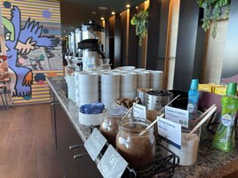 Estação de café com diferentes máquinas de café, saquinhos de açúcar e um aviso indicando a disponibilidade de café.