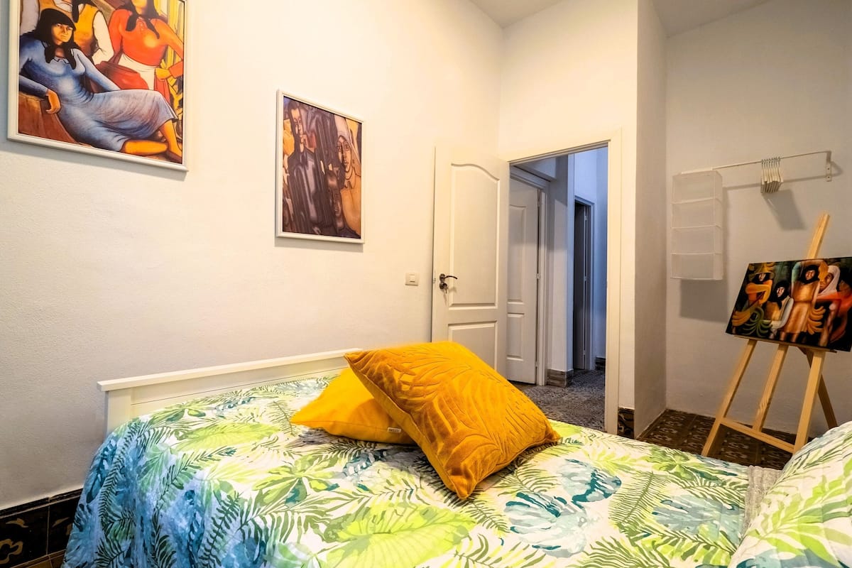 Um quarto com uma cama, um quadro na parede e um cavalete com uma pintura.