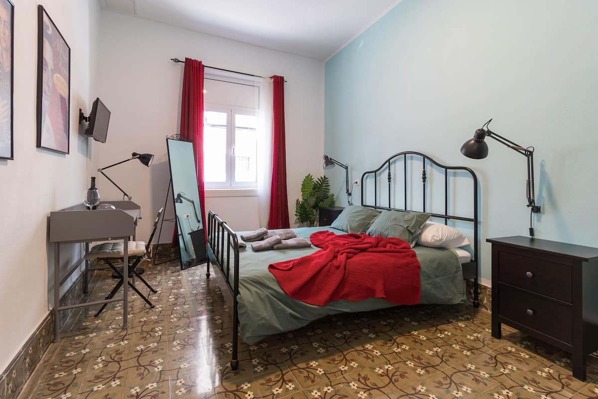 Quarto com cama, mesa de cabeceira, escrivaninha, cadeira e espelho.