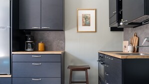 Uma cozinha moderna com armários escuros, um banquinho de madeira e um quadro na parede.