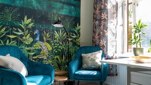 Quarto com cadeiras cor de verde-água, uma mesa branca e um grande mural na parede com folhagem tropical.