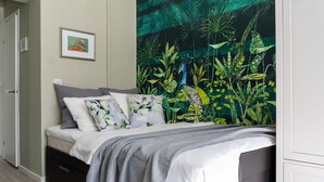 Quarto com cama, almofadas, manta e um mural na parede com um pavão entre plantas.