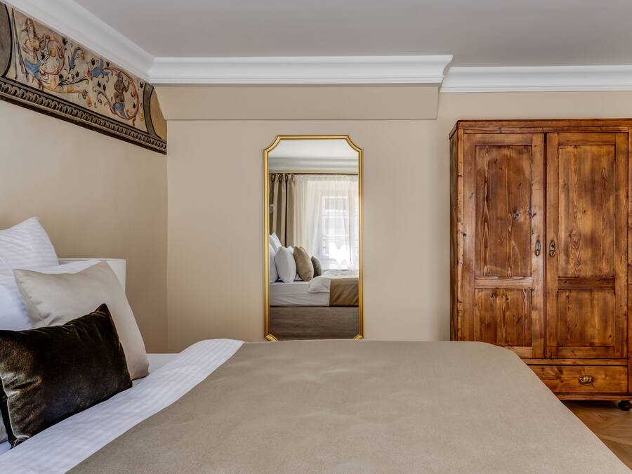 Quarto com cama grande, guarda-roupa de madeira e espelho refletindo o aposento.