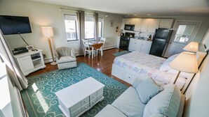 Quarto de hotel compacto com cama, sofá, pequena mesa de jantar, cozinha compacta e televisão.