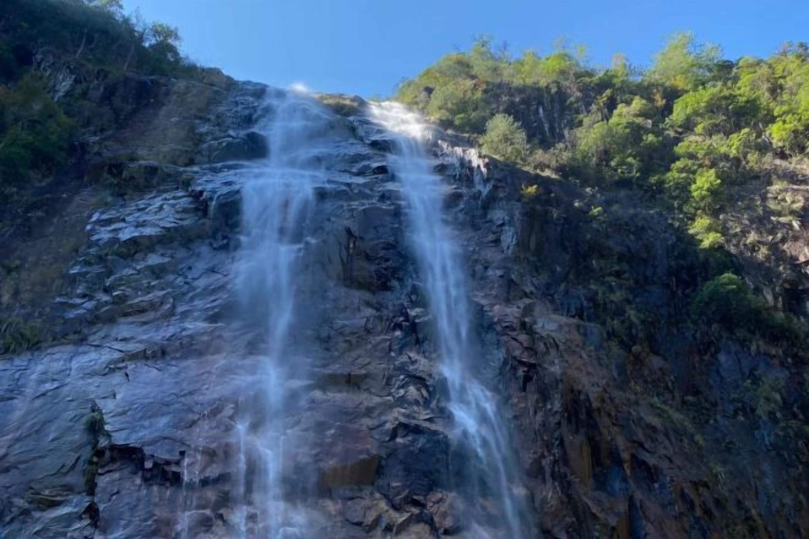 Uma cascata despencando por um penhasco rochoso, rodeada por vegetação densa.