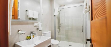 Um banheiro moderno com uma pia grande e branca, vaso sanitário e chuveiro com box de vidro.