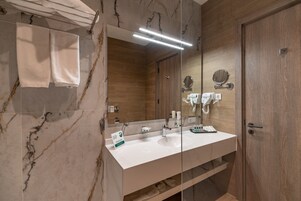 Uma casa de banho moderna com parede de mármore, lavatório branco, espelho e porta de madeira.
