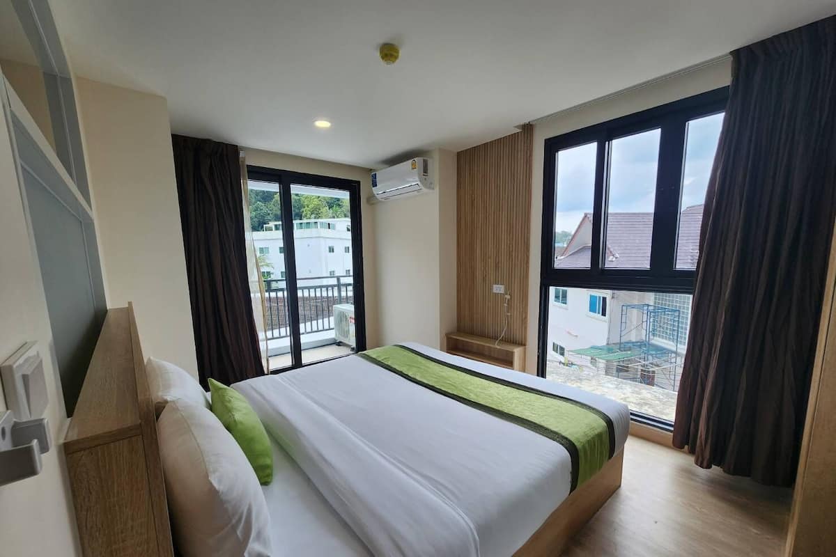 Quarto de hotel com uma cama grande, um guarda-roupa de madeira, uma janela com vista para edifícios e um aparelho de ar condicionado.