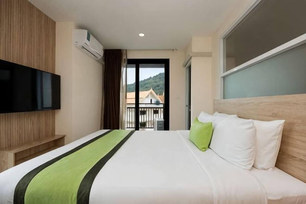 Quarto de hotel com uma cama, uma TV fixada na parede, uma varanda com vista para edifícios e um aparelho de ar condicionado.