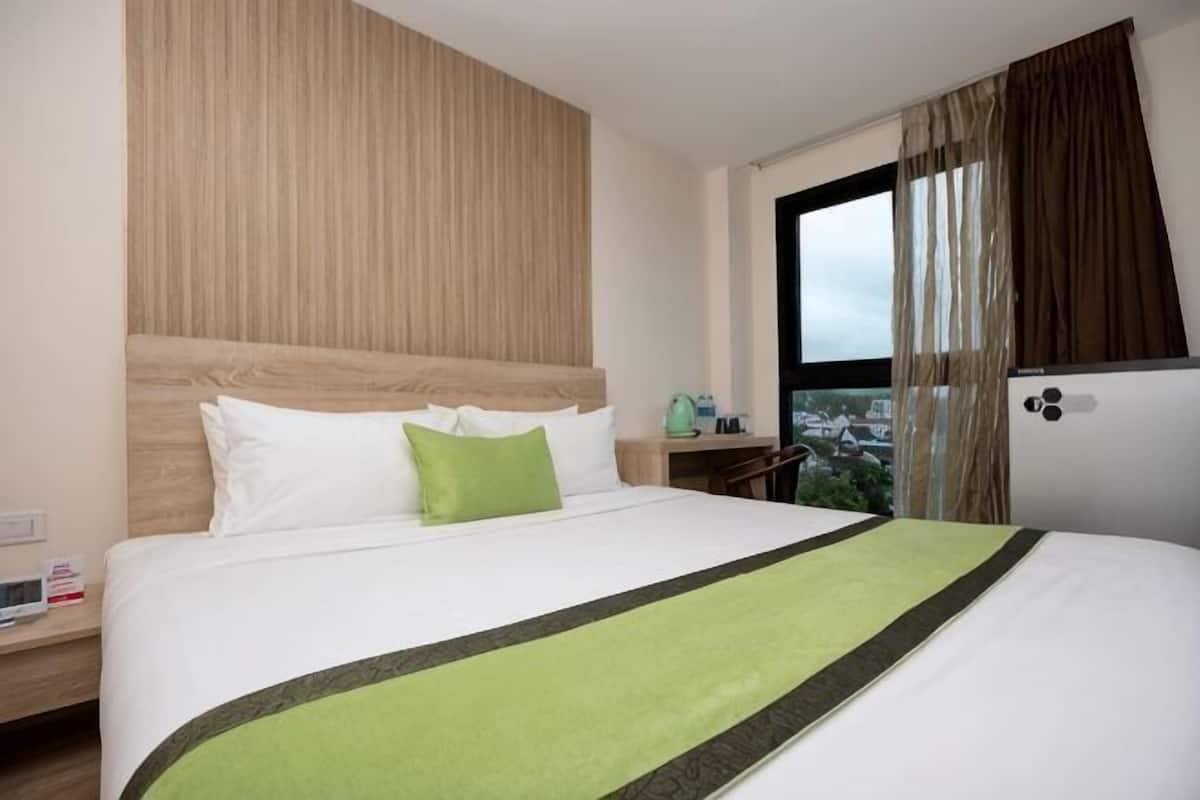 Quarto de hotel com uma cama grande, cabeceira de madeira, mesa de cabeceira, janela com cortinas e vista da cidade.