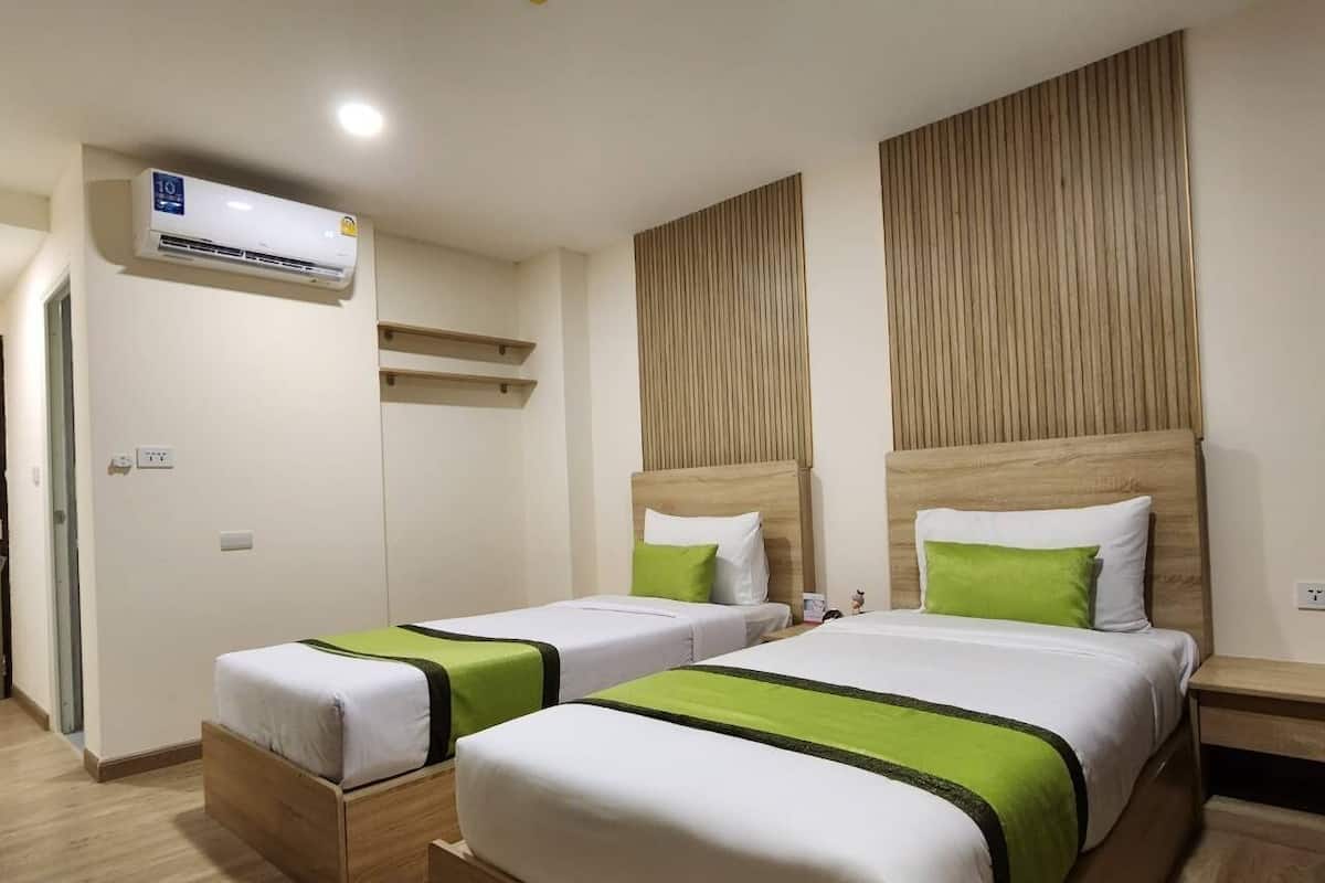 Quarto de hotel com duas camas de solteiro, cabeceira de madeira, ar condicionado fixado na parede e piso de madeira.