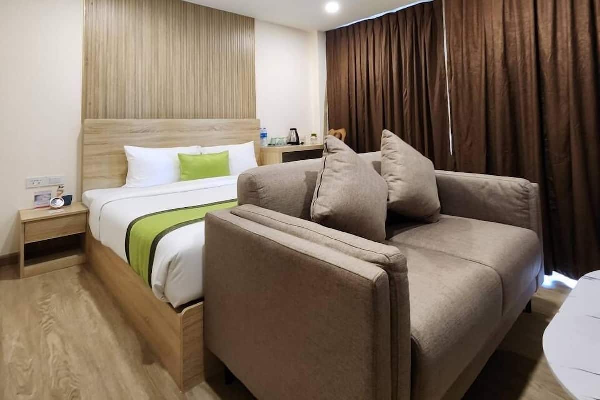 Quarto de hotel com cama, sofá, mesa de cabeceira e uma pequena mesa com cadeira.