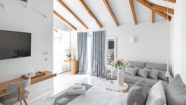 Uma sala de estar moderna com teto de madeira, televisão de tela plana, sofá, mesa de centro e um espaço de jantar com um banco de madeira e uma bandeja com copos.