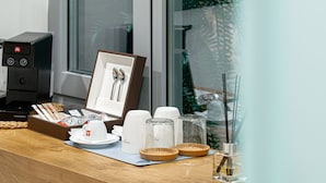 Um pequeno-almoço bem arrumado com uma máquina de café, chávenas e uma moldura com uma fotografia sobre uma mesa de madeira perto de uma janela.