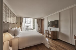 Quarto de hotel com uma cama grande, televisão, piso de madeira e varanda com cortinas.