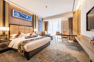 Quarto de hotel com uma cama grande, uma escrivaninha, uma cadeira e uma televisão.