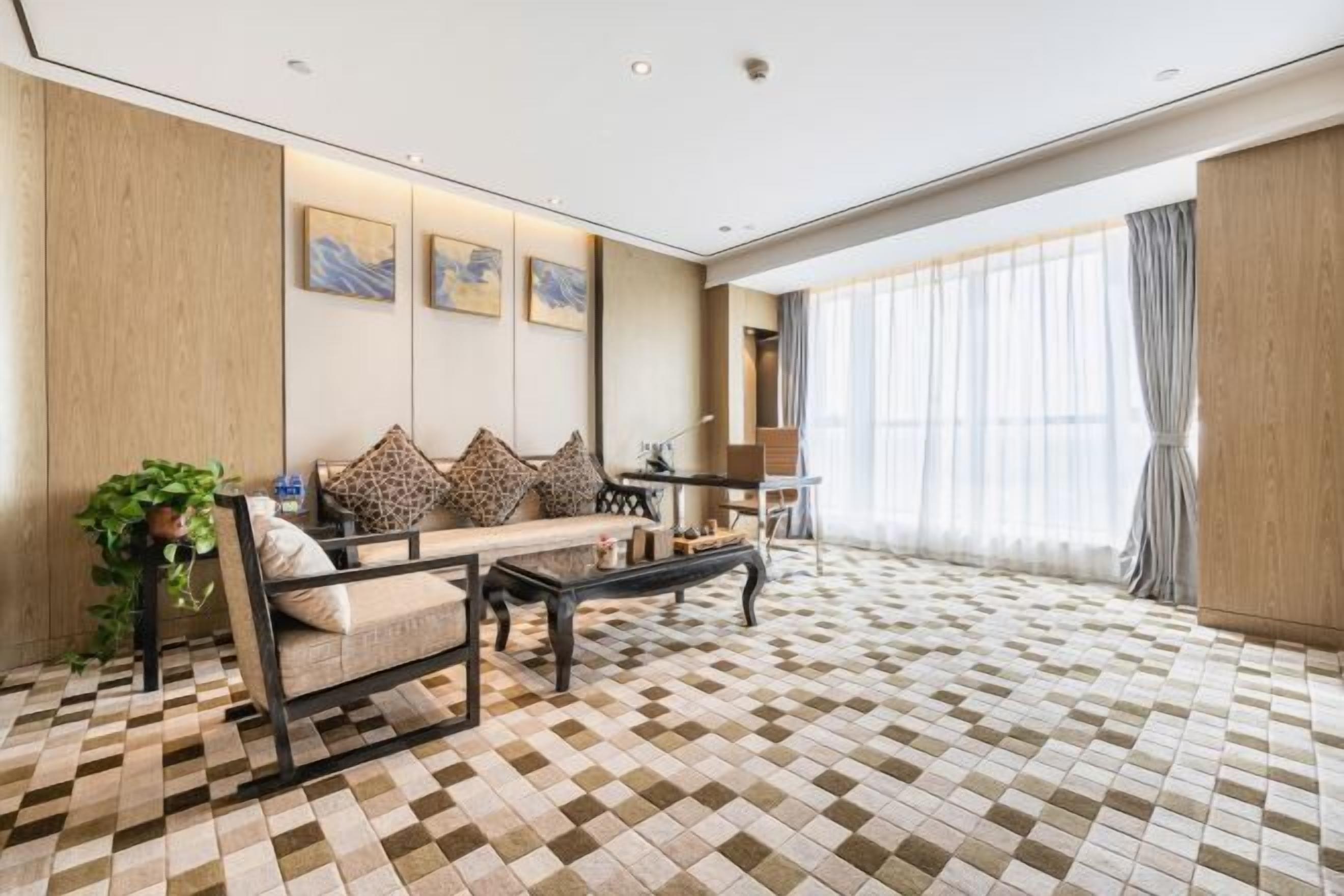 Quarto de hotel com chão xadrez, um sofá, uma mesa de centro, uma escrivaninha e uma janela grande com cortinas.