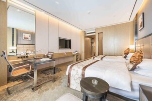 Quarto de hotel moderno com uma cama grande, uma escrivaninha, uma cadeira, uma televisão e um espelho.