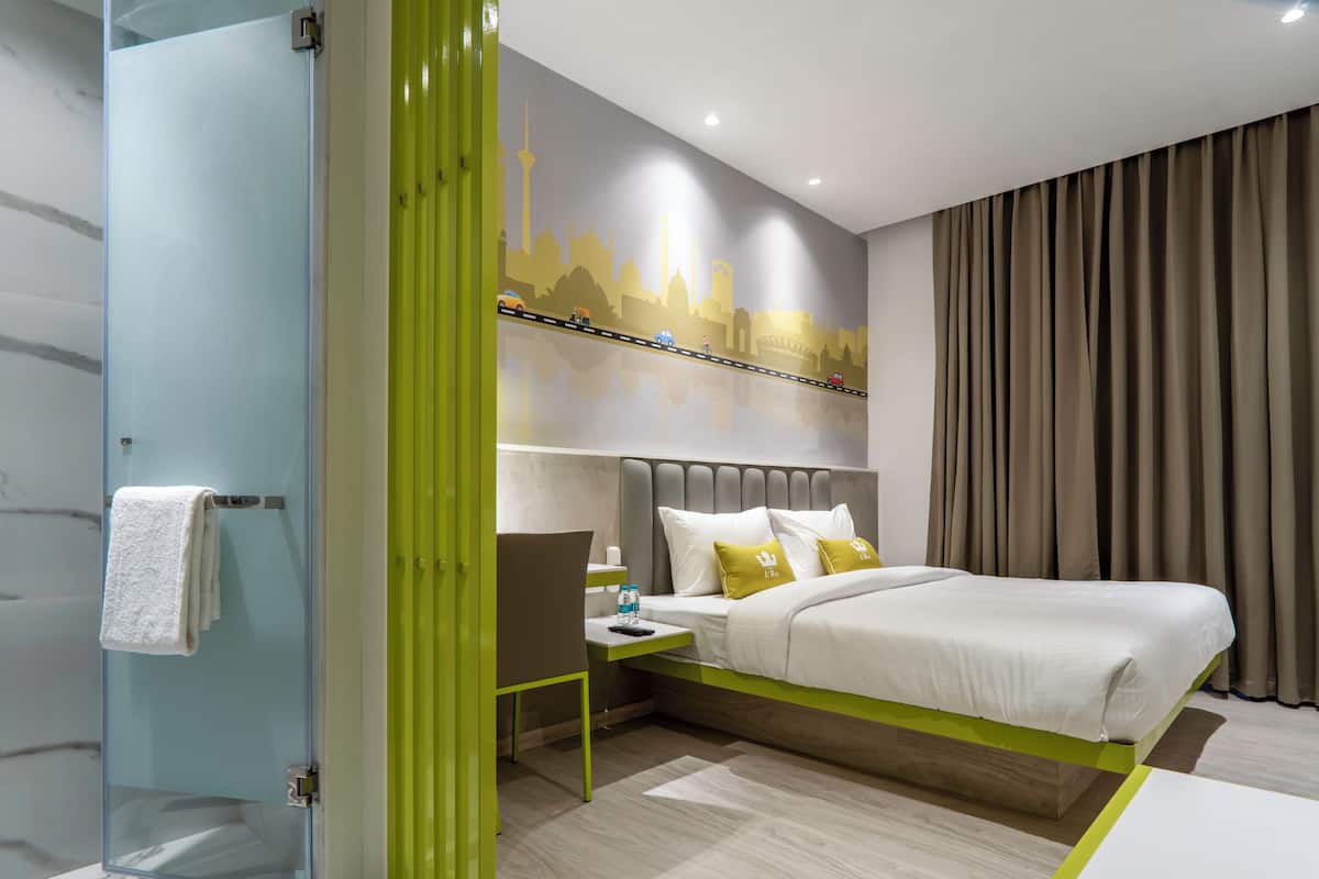 Quarto de hotel moderno com cama, mesa de cabeceira e área de chuveiro.