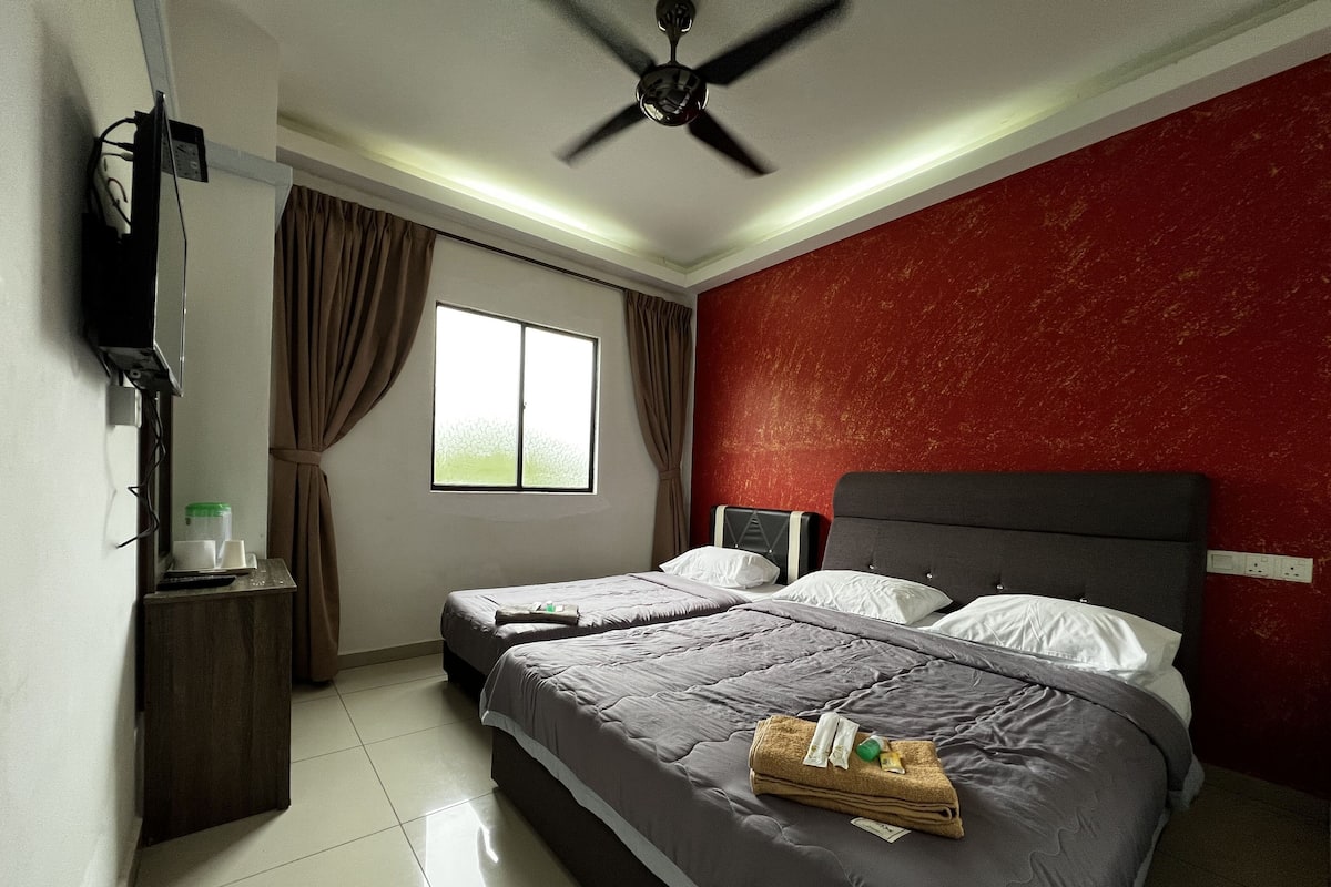 Quarto de hotel com cama, escrivaninha, ventoinha no teto e janela com cortinas.