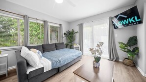Uma sala de estar moderna com um sofá cinza, uma mesa de centro de madeira e uma TV na parede exibindo 