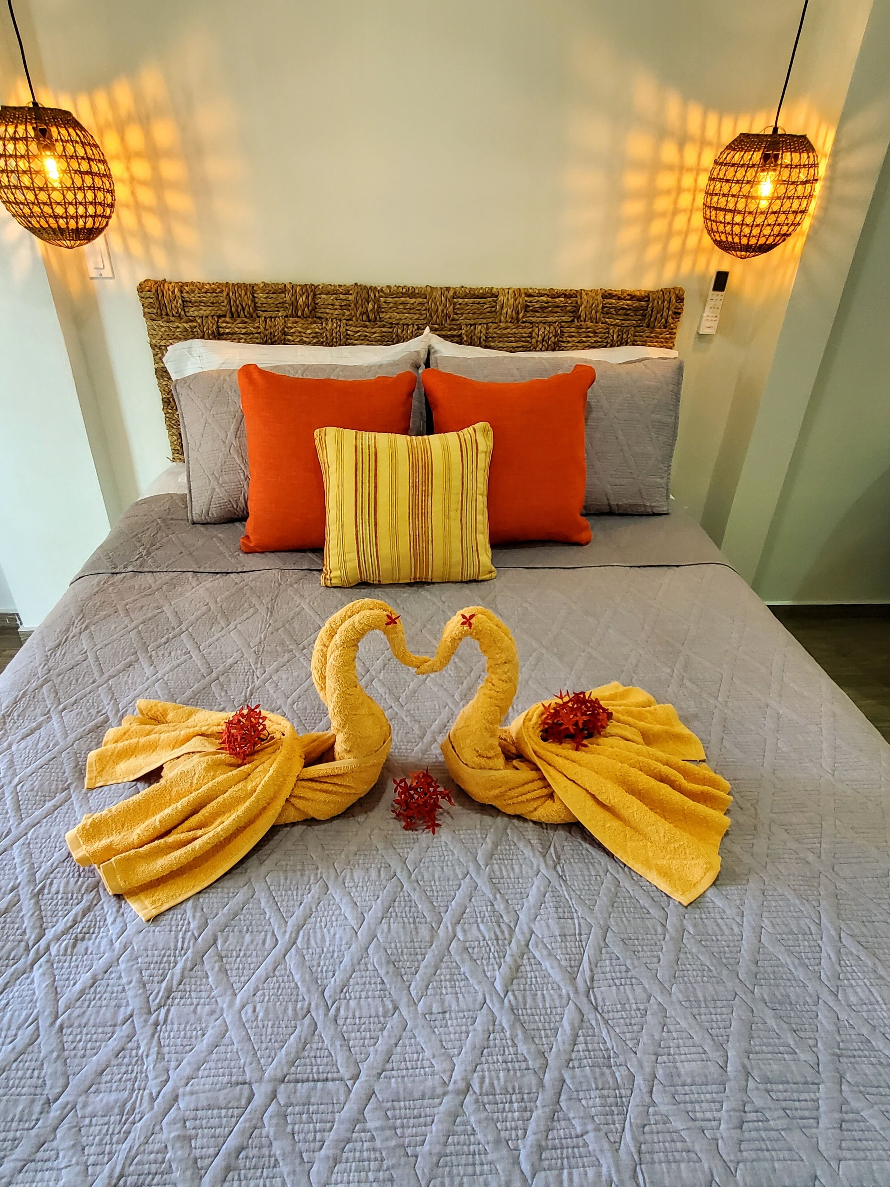 Uma cama com colcha acolchoada, duas toalhas em formato de cisne e cabeceira de fibra natural.