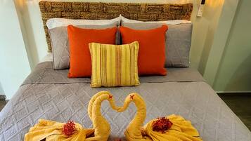 Uma cama com colcha acolchoada, duas toalhas em formato de cisne e cabeceira de fibra natural.