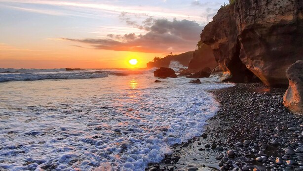 Uma praia com seixos e ondas ao pôr do sol.