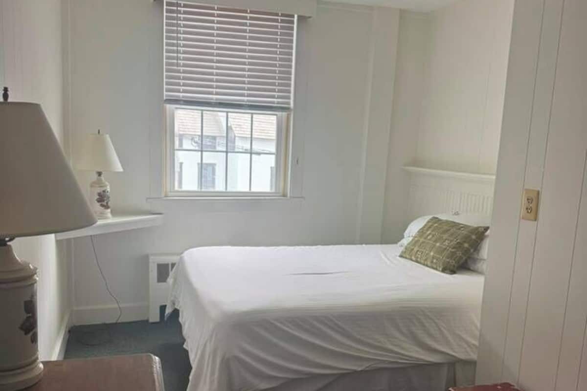 Quarto pequeno com uma cama de solteiro, janela, escrivaninha e cadeira.