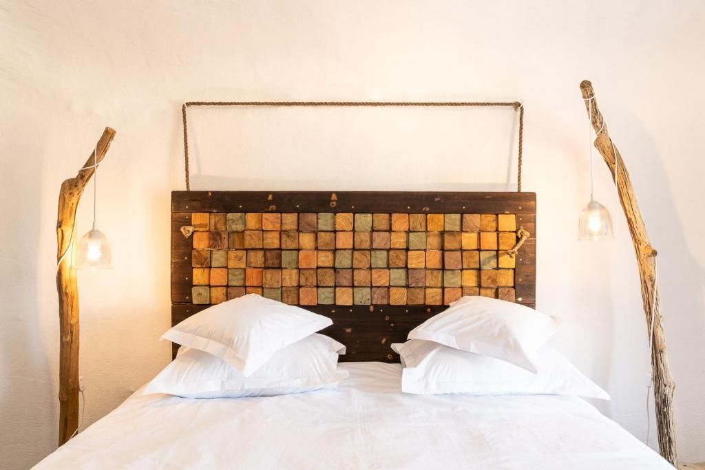 Uma cama com cabeceira de madeira com padrão de mosaico, ladeada por dois ramos de madeira com luzes penduradas.