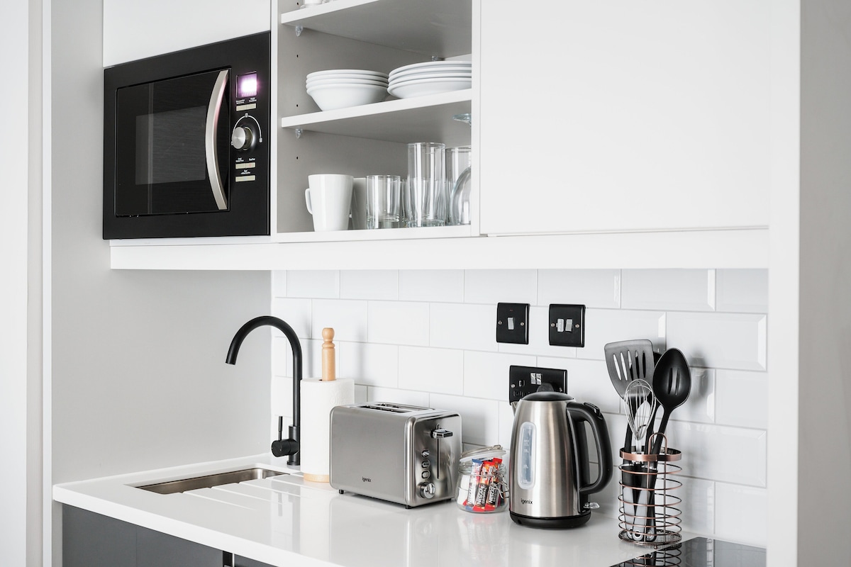 Uma cozinha moderna com micro-ondas embutido, torradeira, chaleira e suporte para utensílios.