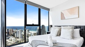 Quarto de hotel moderno com cama grande, vista da cidade e paisagem urbana através de janelas do chão ao teto.