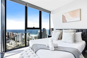 Quarto de hotel moderno com cama grande, vista da cidade e paisagem urbana através de janelas do chão ao teto.