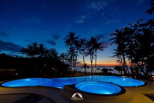 Área de piscina com várias piscinas circulares, cercada por palmeiras e vista para o pôr do sol.