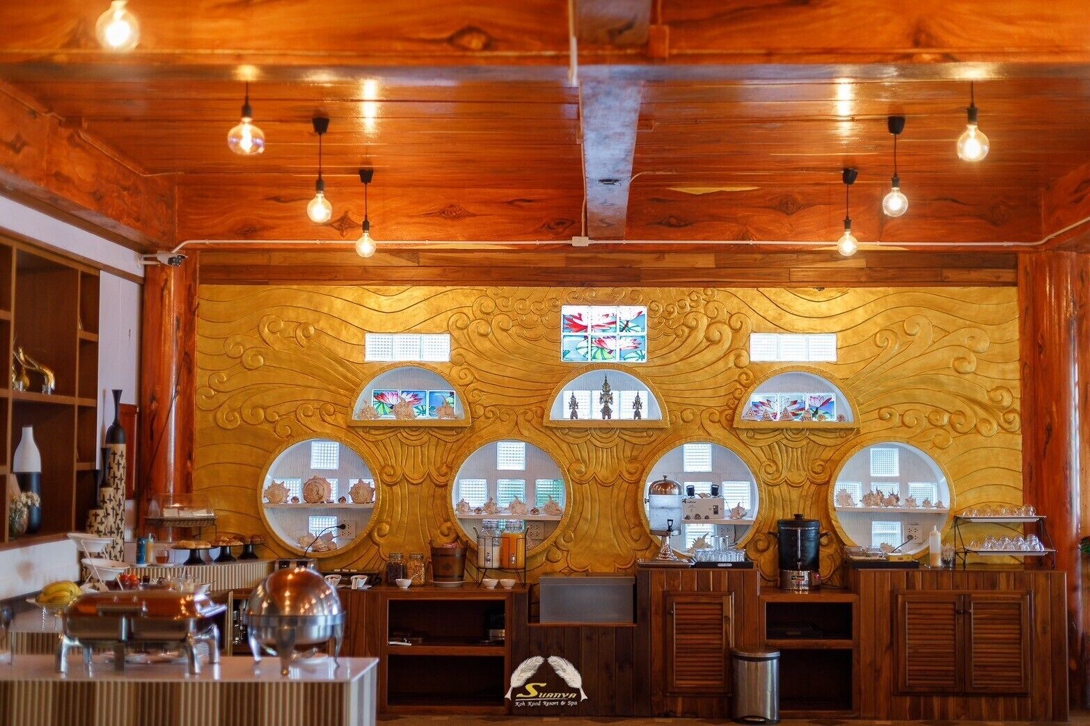 Interior de restaurante com paredes de madeira, lâmpadas pendentes e espelhos decorativos.