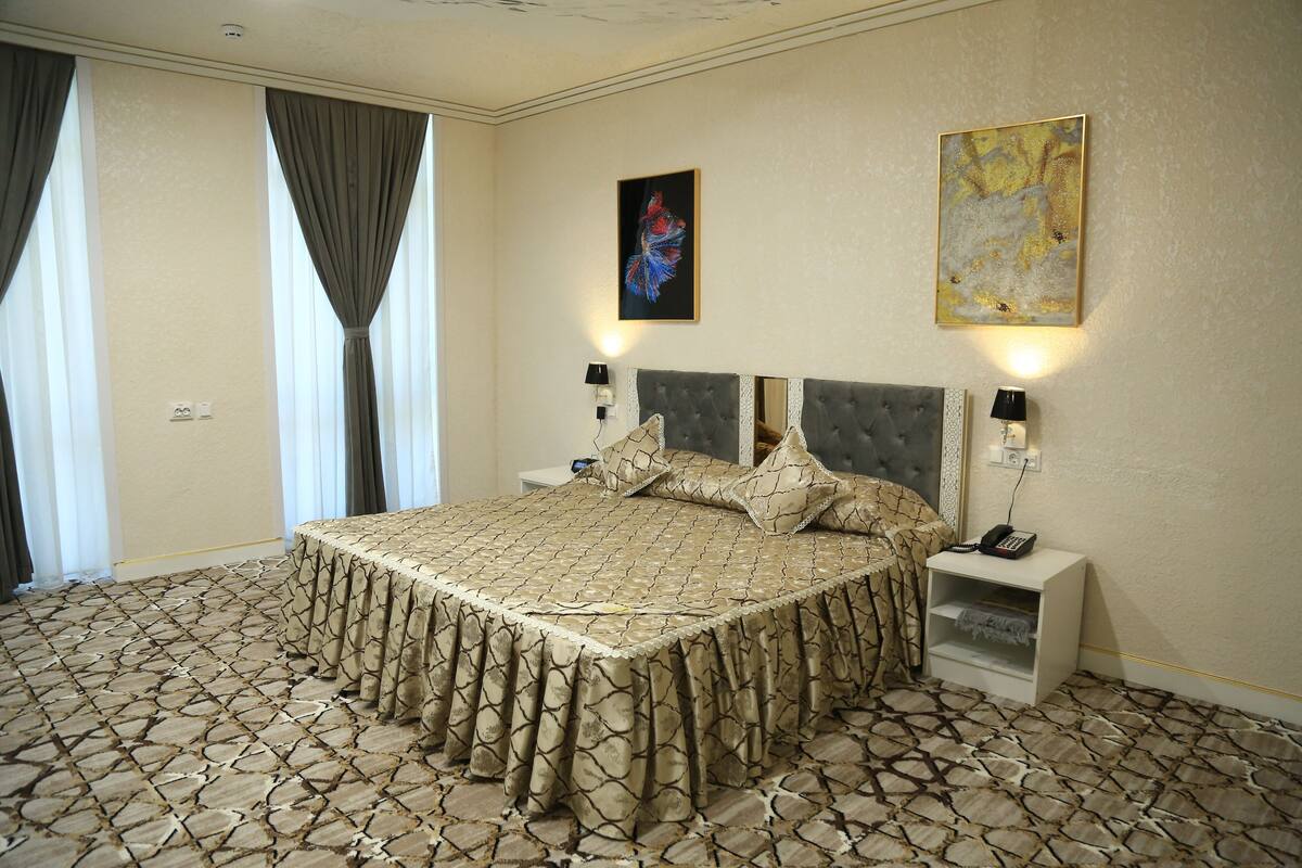 Quarto de hotel com uma cama grande, duas mesas de cabeceira, um criado-mudo, um telefone fixado na parede e um quadro.